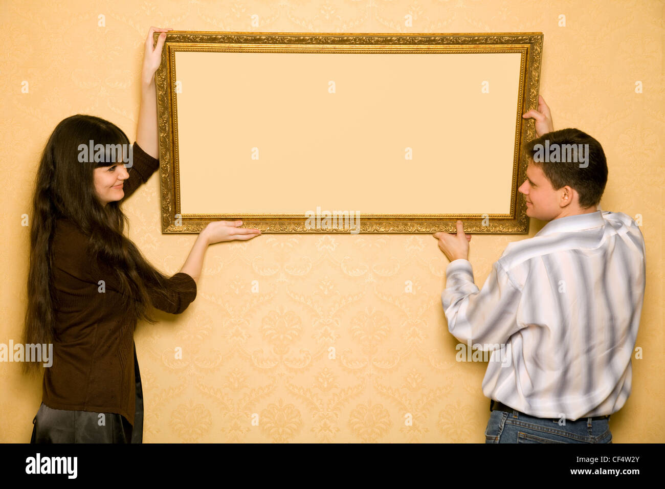 young beautiful woman and smiling man hang up on wall picture in frame ...