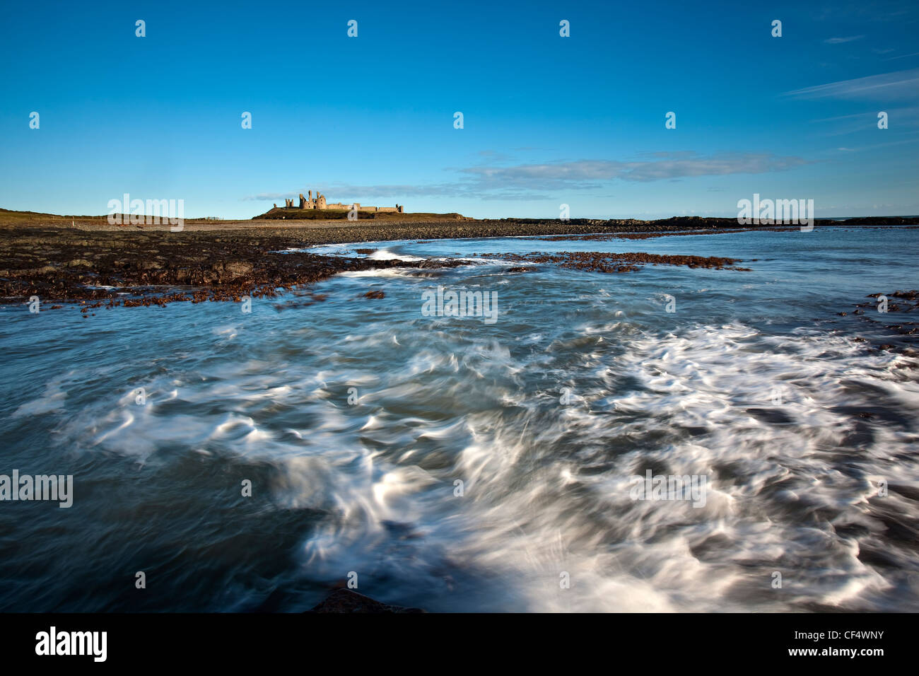 The remains of Dunstanburgh Castle built on a headland dominating a ...