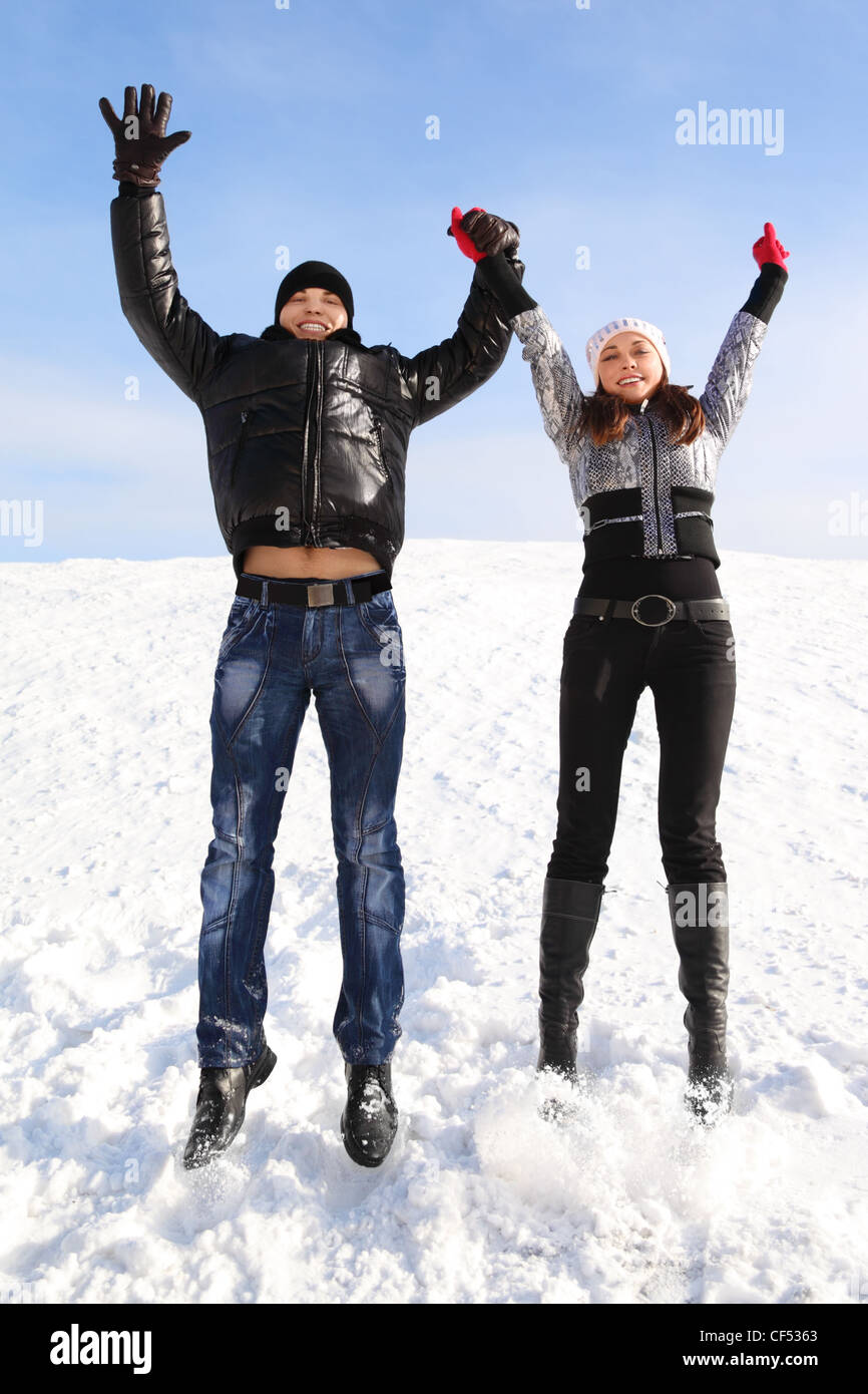 young man and girl jump on snowy area and smiling, holding for hands ...