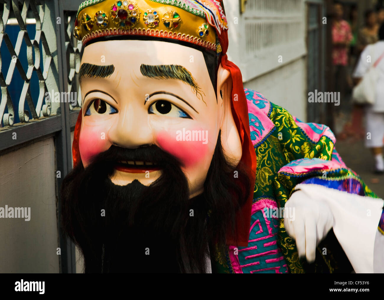 Man in Chinese costume with papier-mache head and beard carried in ...