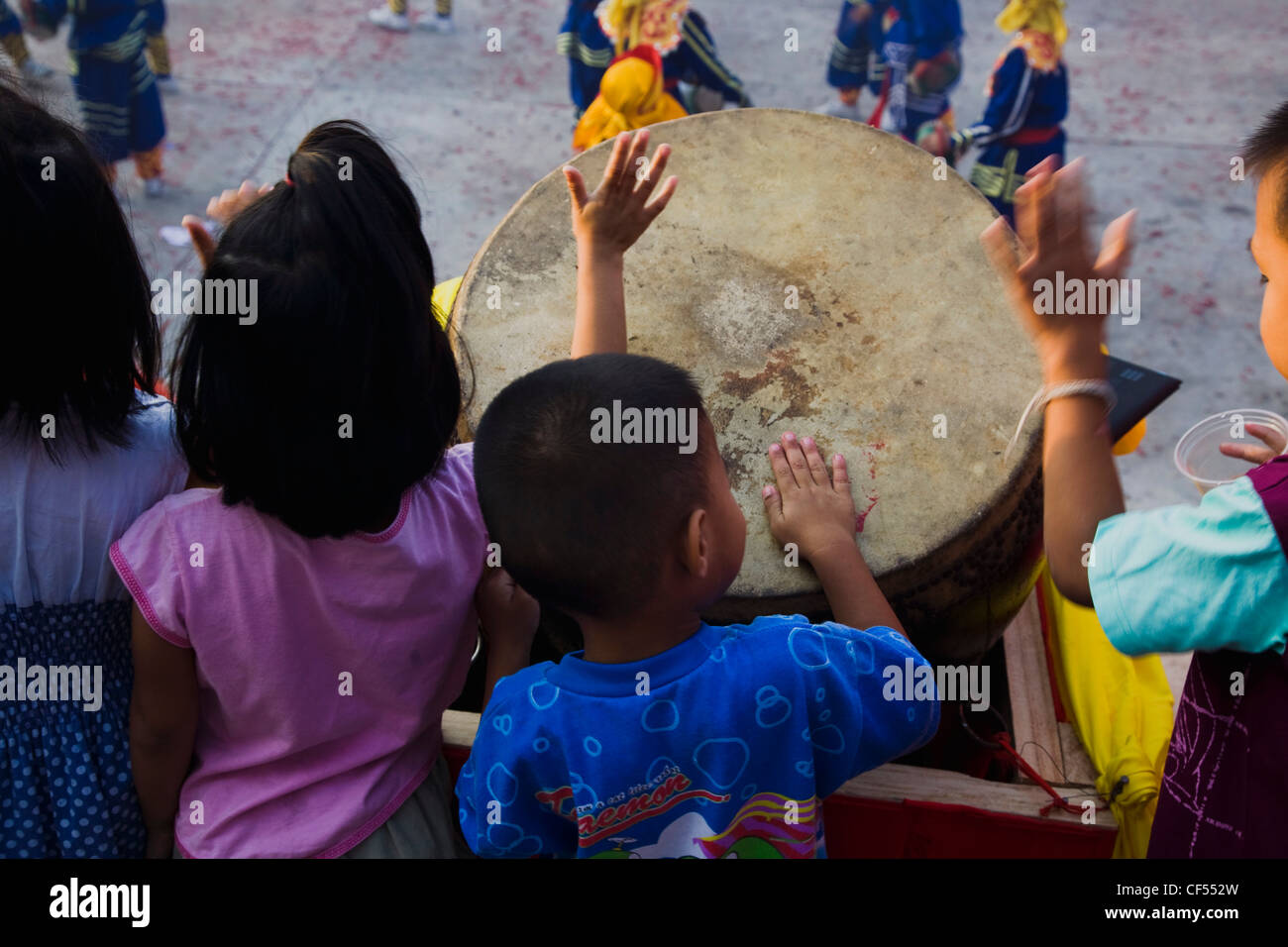 Thai children bang drum while watching dance troupe with firecrackers ...