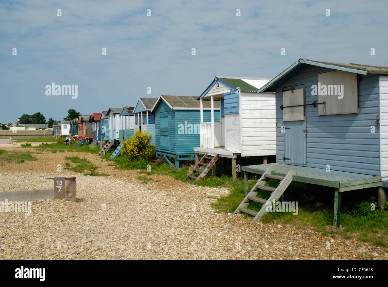 A row of colourful seafront beach huts and shingle beach in Whitstable ...