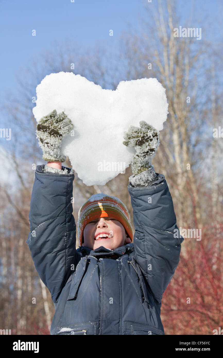 boy keeps in hands hearts from snow over head in winter in wood Stock ...