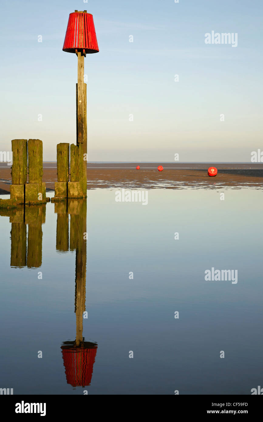 Navigation marker post and timber sea defence groyne at low tide ...