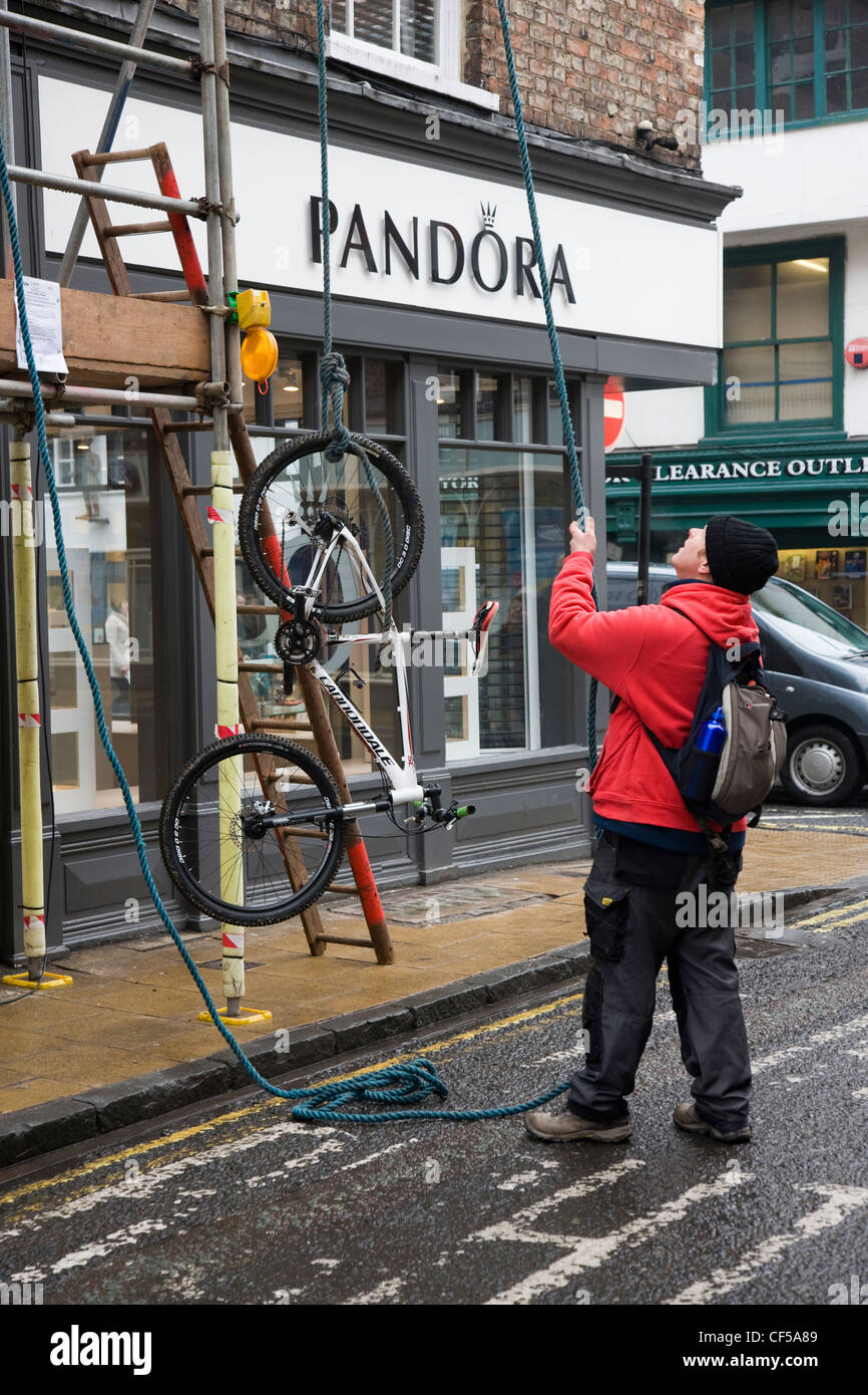 Hoisting a bicycle on the end of a rope to the top of the scaffolding ...