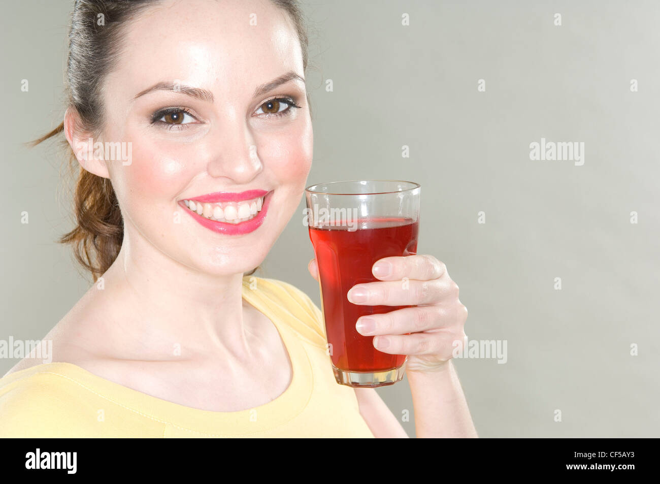 Female wearing yellow top drinking glass of cranberry juice Stock Photo ...