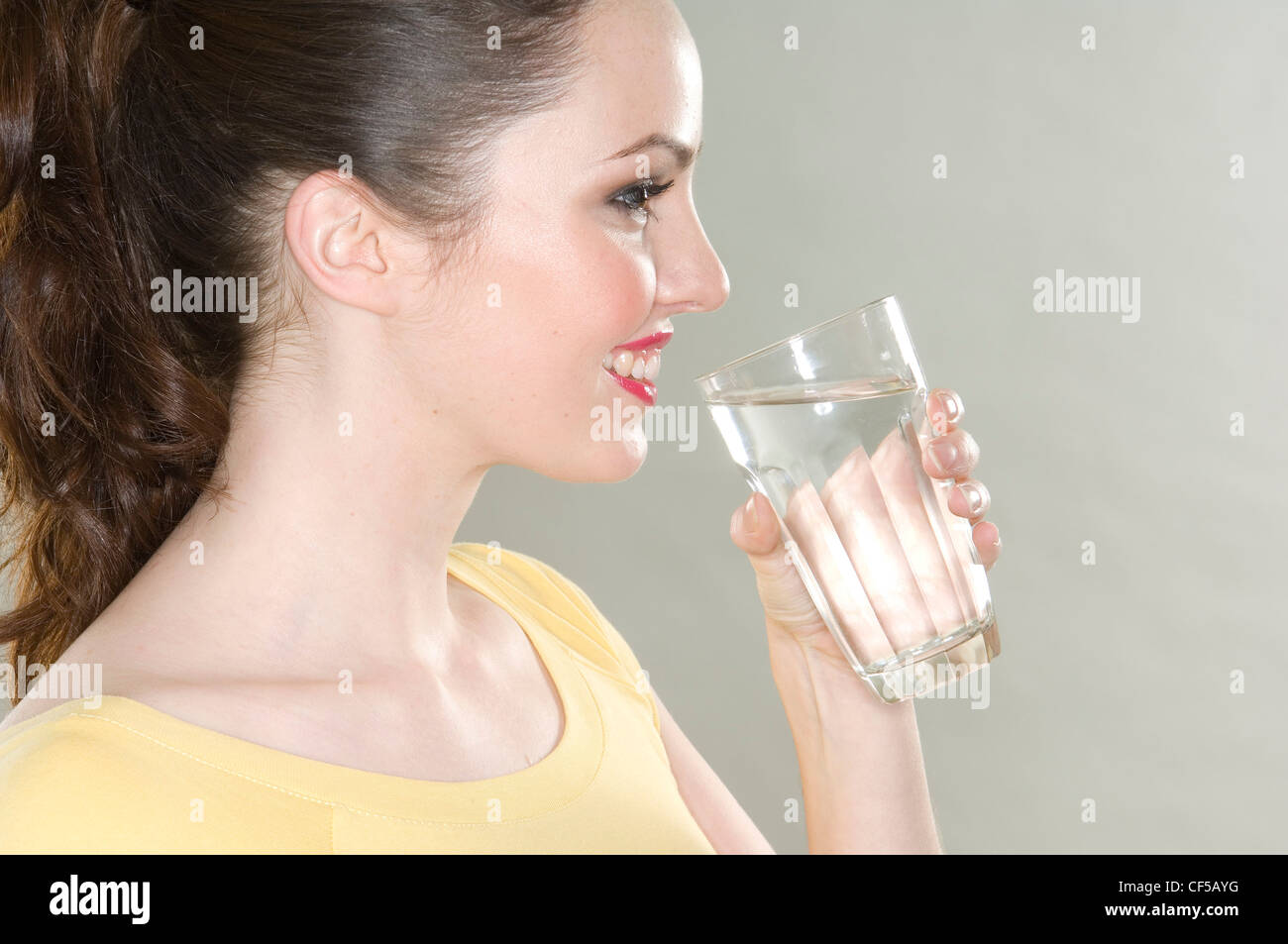 Female wearing yellow top drinking glass of water Stock Photo - Alamy
