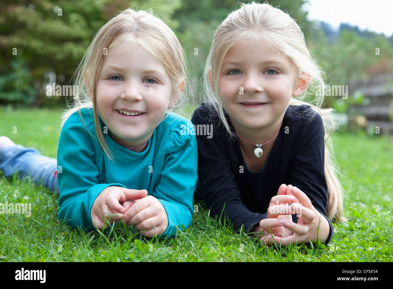 Germany, Bavaria, Huglfing, Girls lying on grass in garden, smiling ...