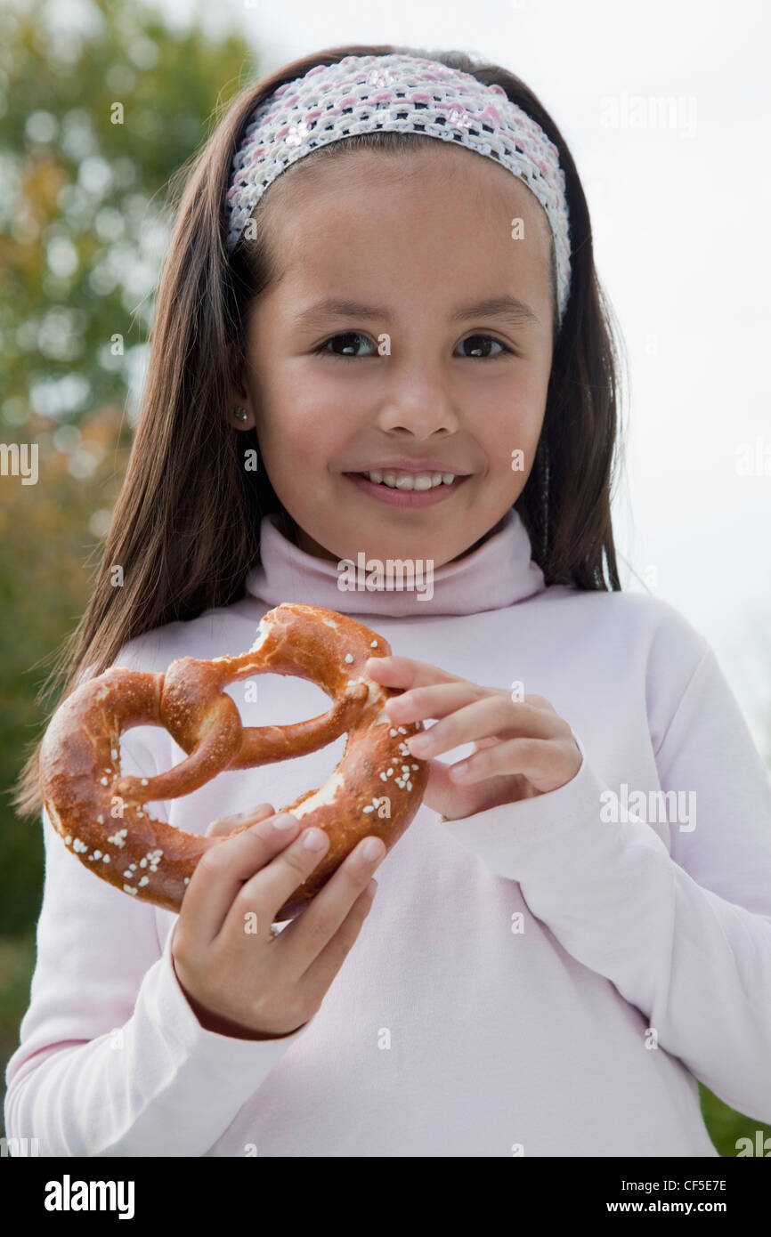 Germany, Bavaria, Huglfing, Girl holding pretzel in garden, smiling ...