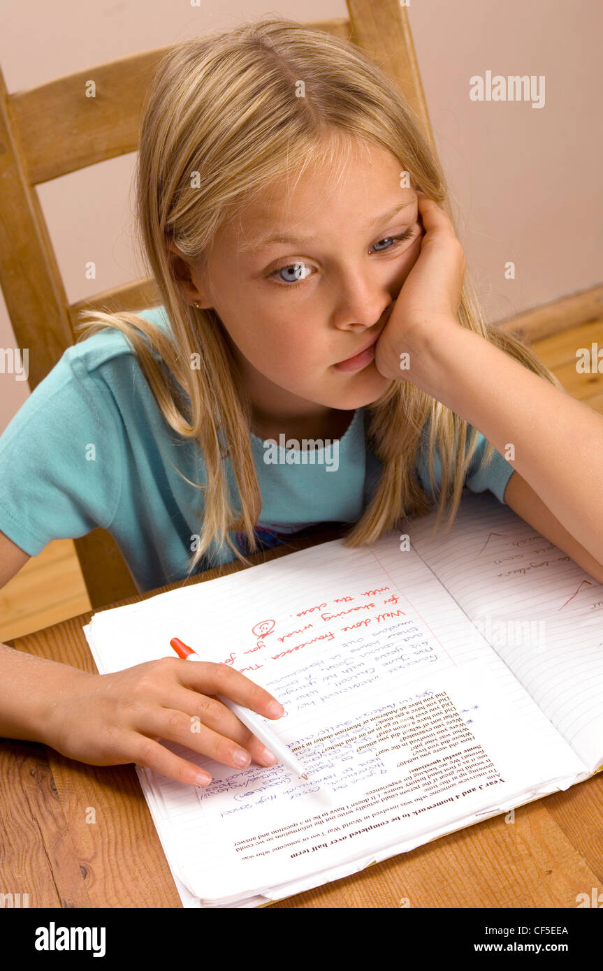 Female child sat at a wooden table doing homework, leaning her head on ...