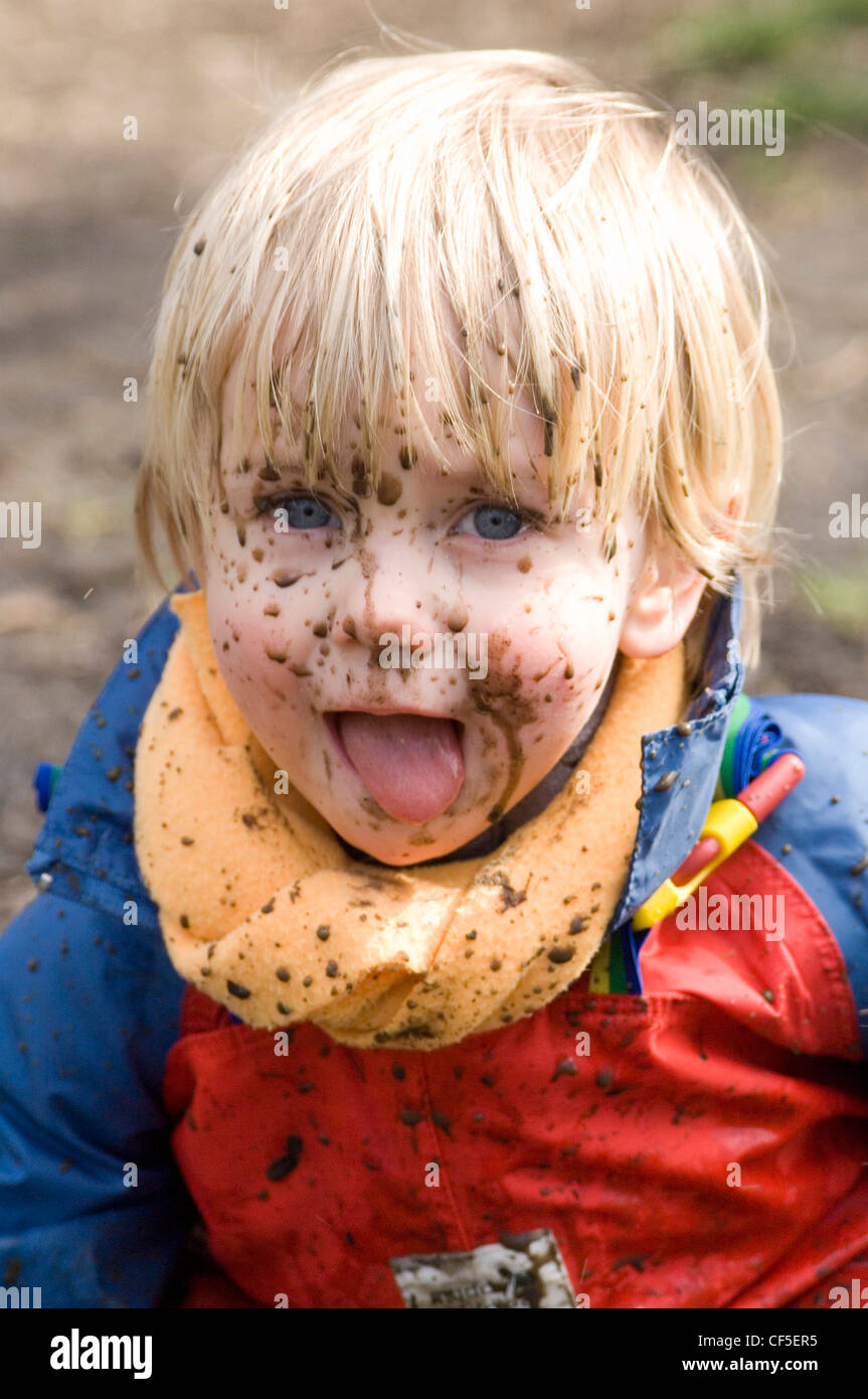 A male child standing by a large muddy puddle with mud splattered over ...