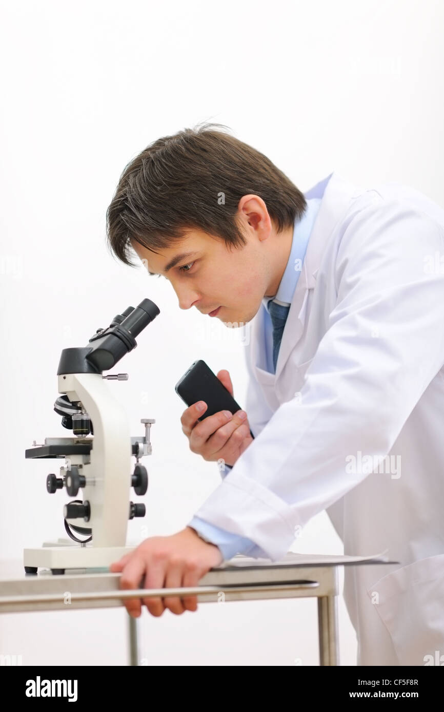Researcher looking in microscope and making notes on voice recorder ...