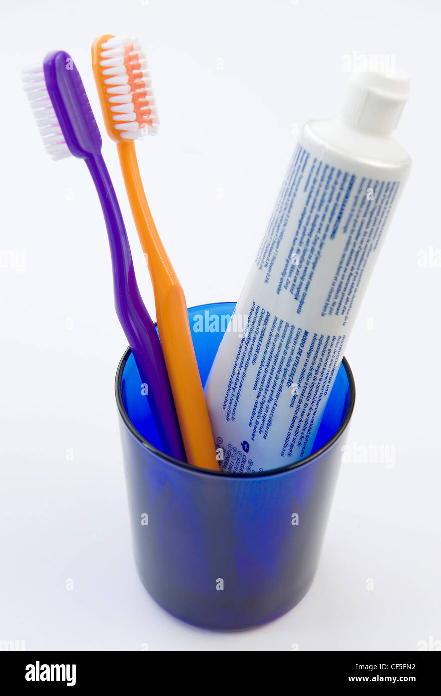 A blue glass with a tube of toothpaste, a purple toothbrush and yellow ...
