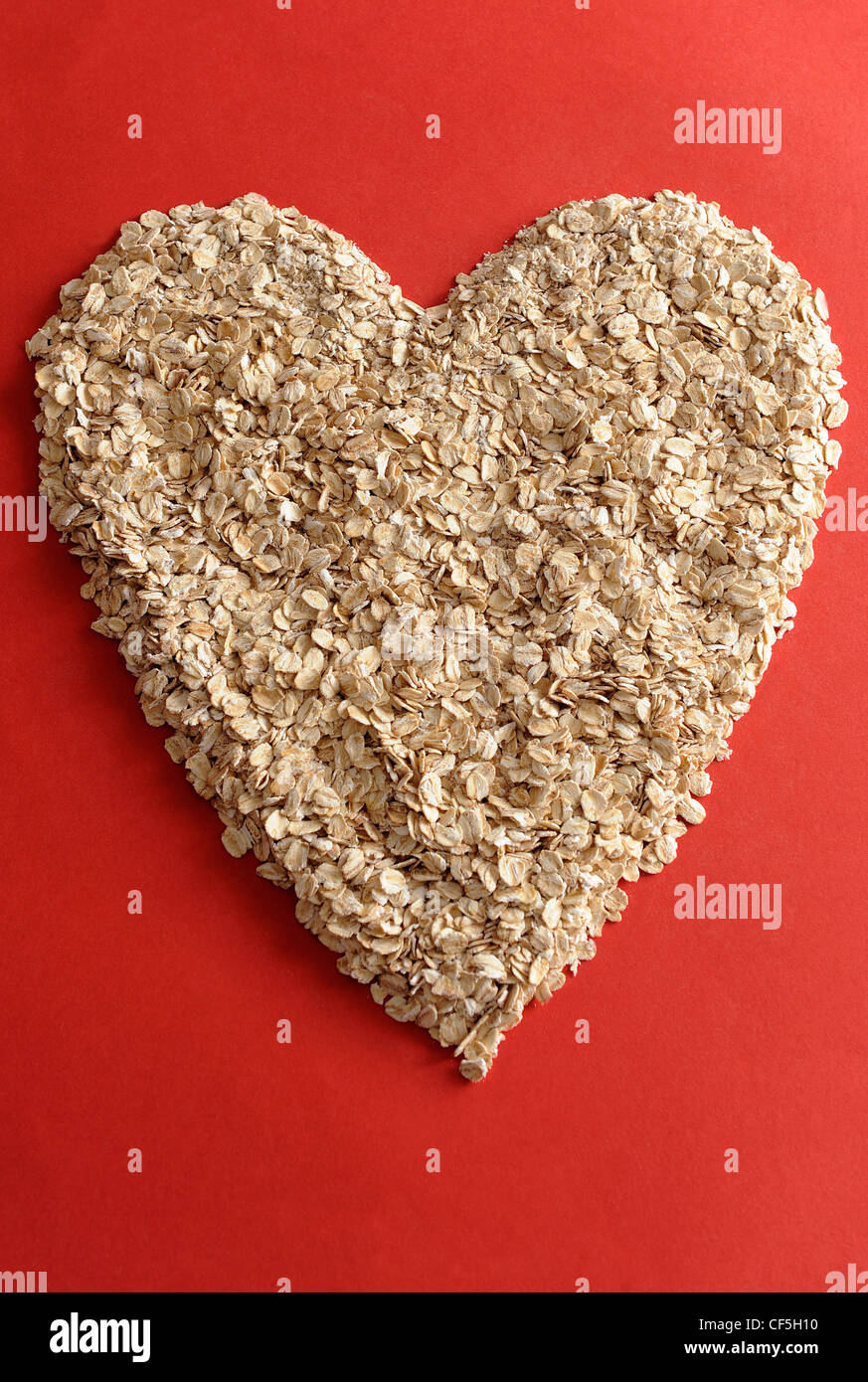 A still life image of dry porridge oats in heart shape on red ...