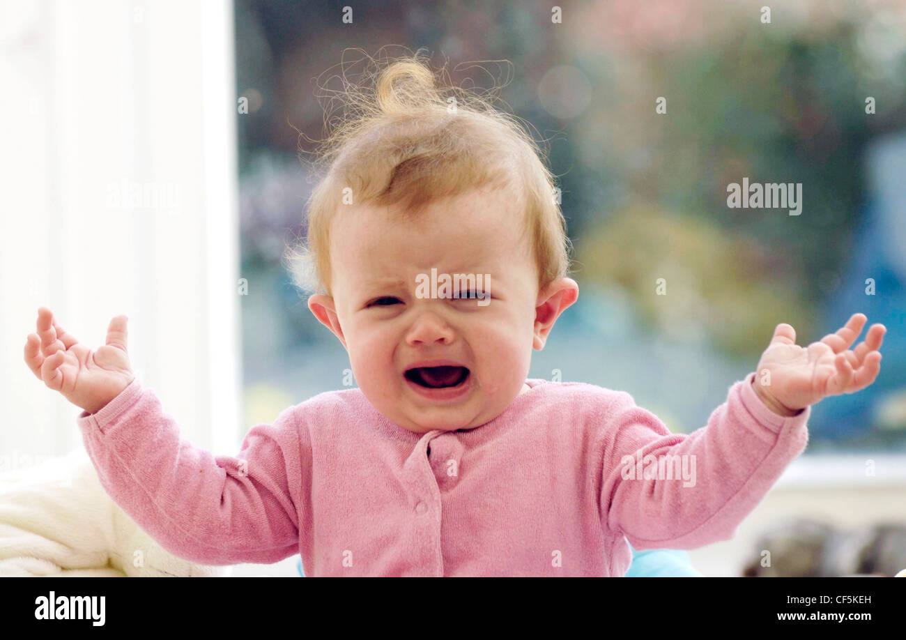 Female baby, months old, wearing a pink babygro, crying with arms up in ...