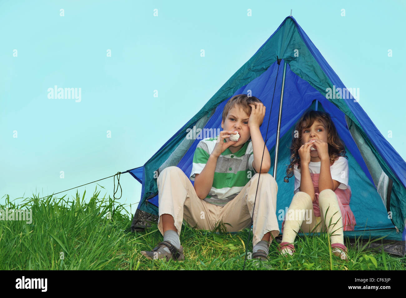 Small children have a rest on the nature, sit near tent and eat sweets ...