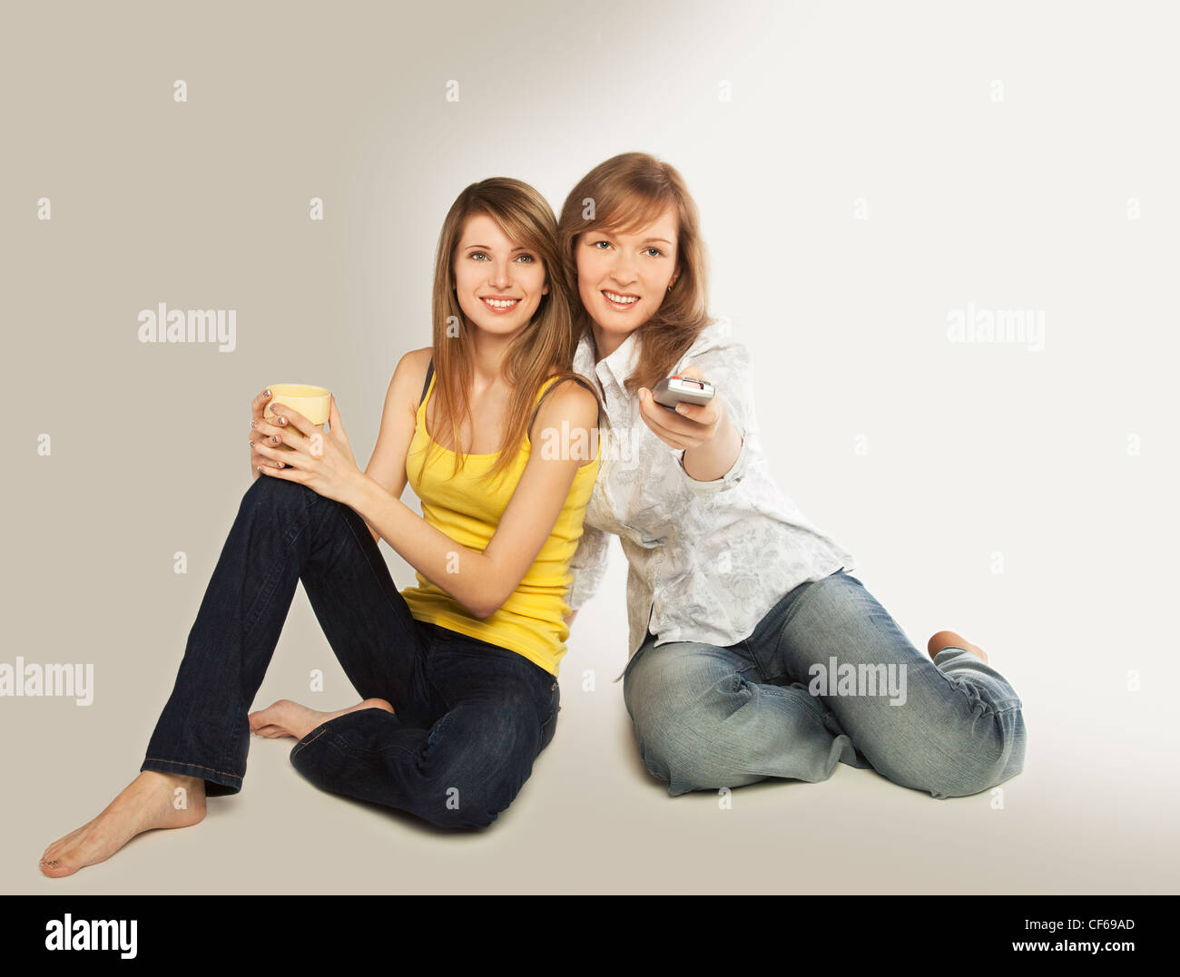 Two smiling pretty blond girls watch TV; isolated on white background ...