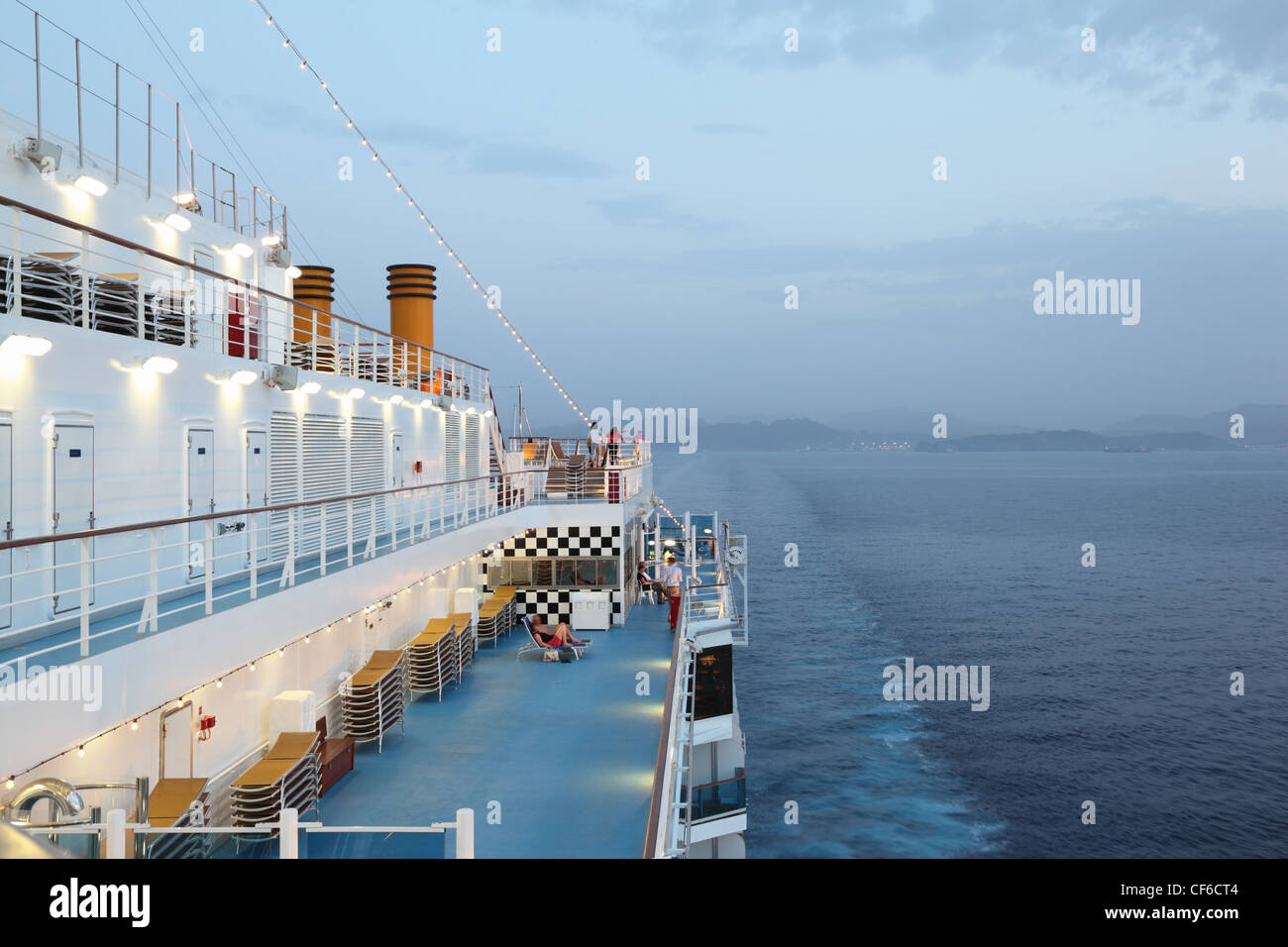 big cruise ship riding in evening. light on. few of people on deck of ...