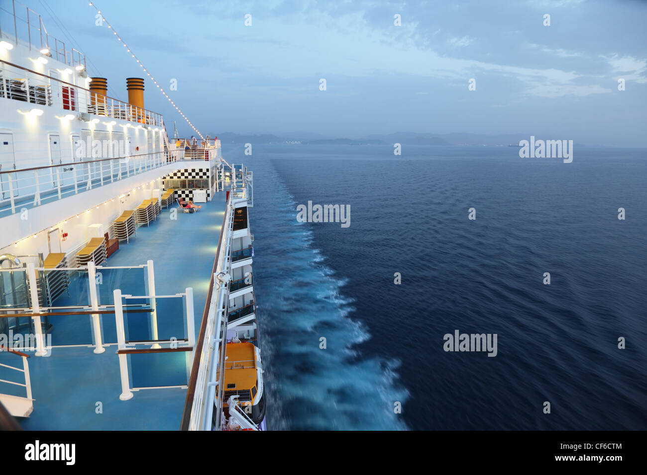 big cruise ship riding in evening. light on. few of people on deck ...
