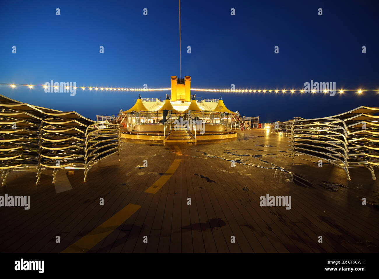 illuminated deck of cruise ship at evening. bar and tables in center of ...