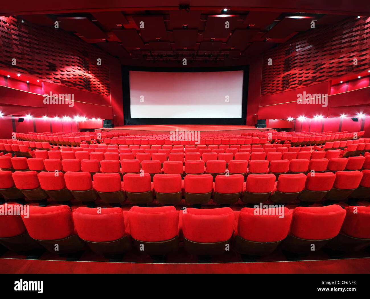 Rows of comfortable red chairs towards to big screen in illuminate red ...