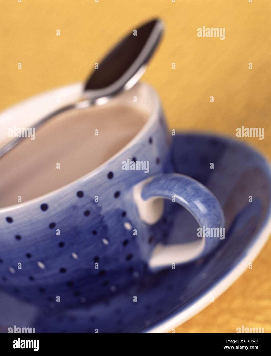 Cropped blue and navy spotted cup and saucer containing tea silver ...