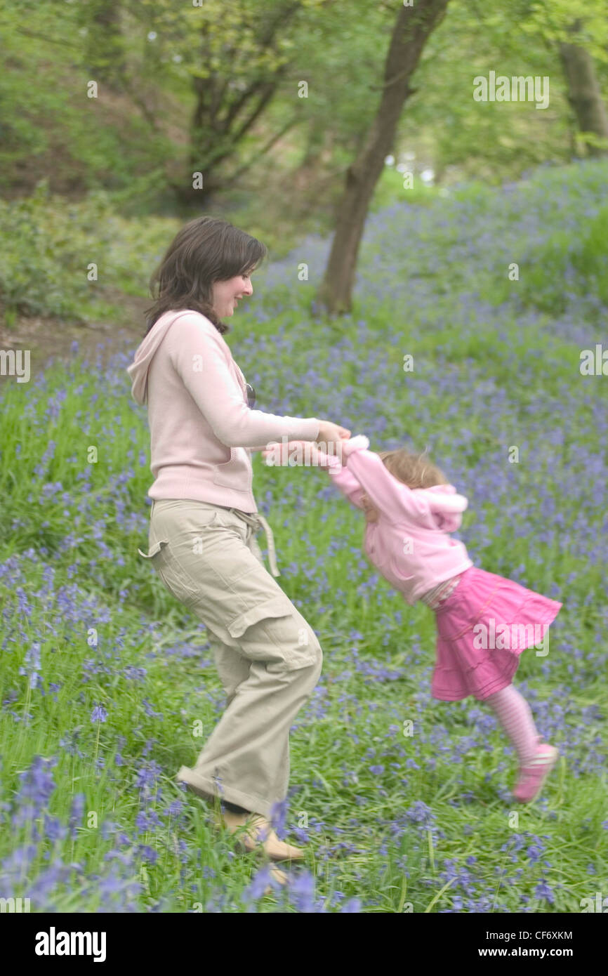 Female swinging child round in air by arms in field of bluebells in ...