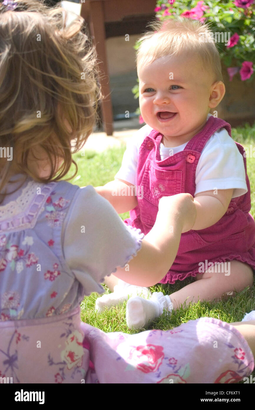 Female baby and female child sitting on grass lawn facing each other ...