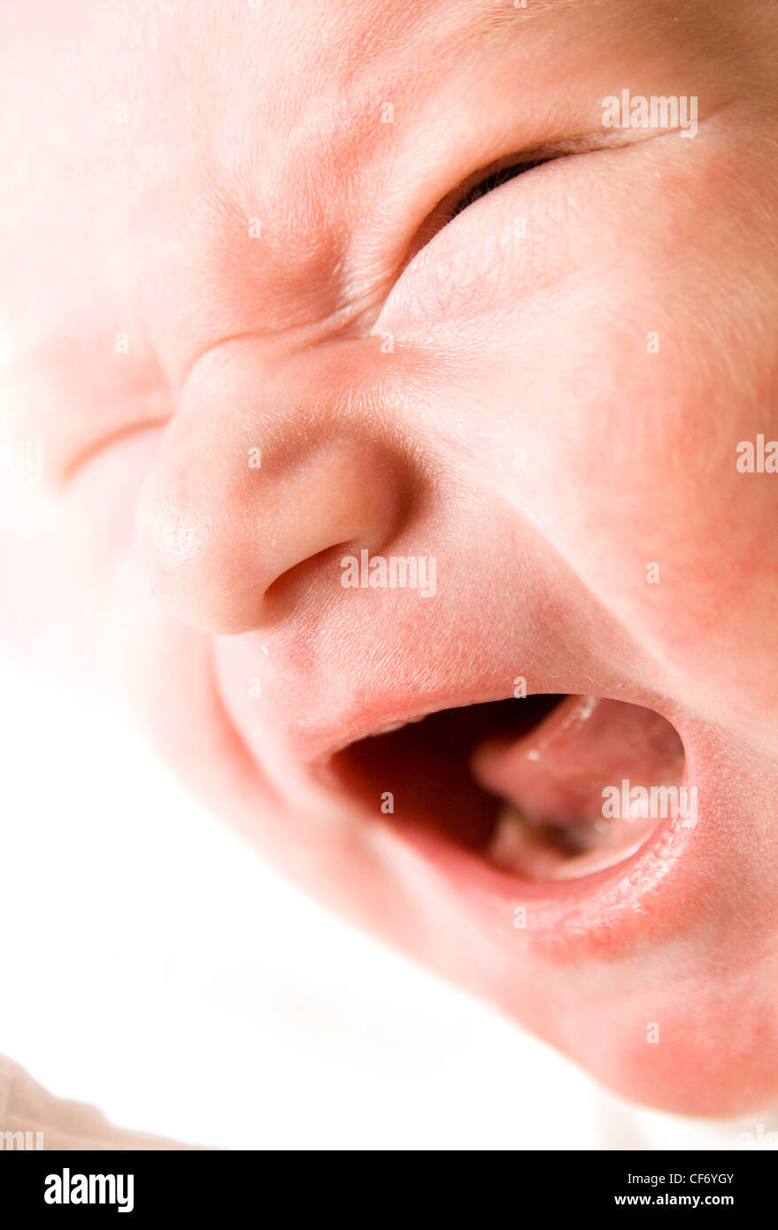 Close up of new born baby screaming with eyes shut and mouth wide open ...