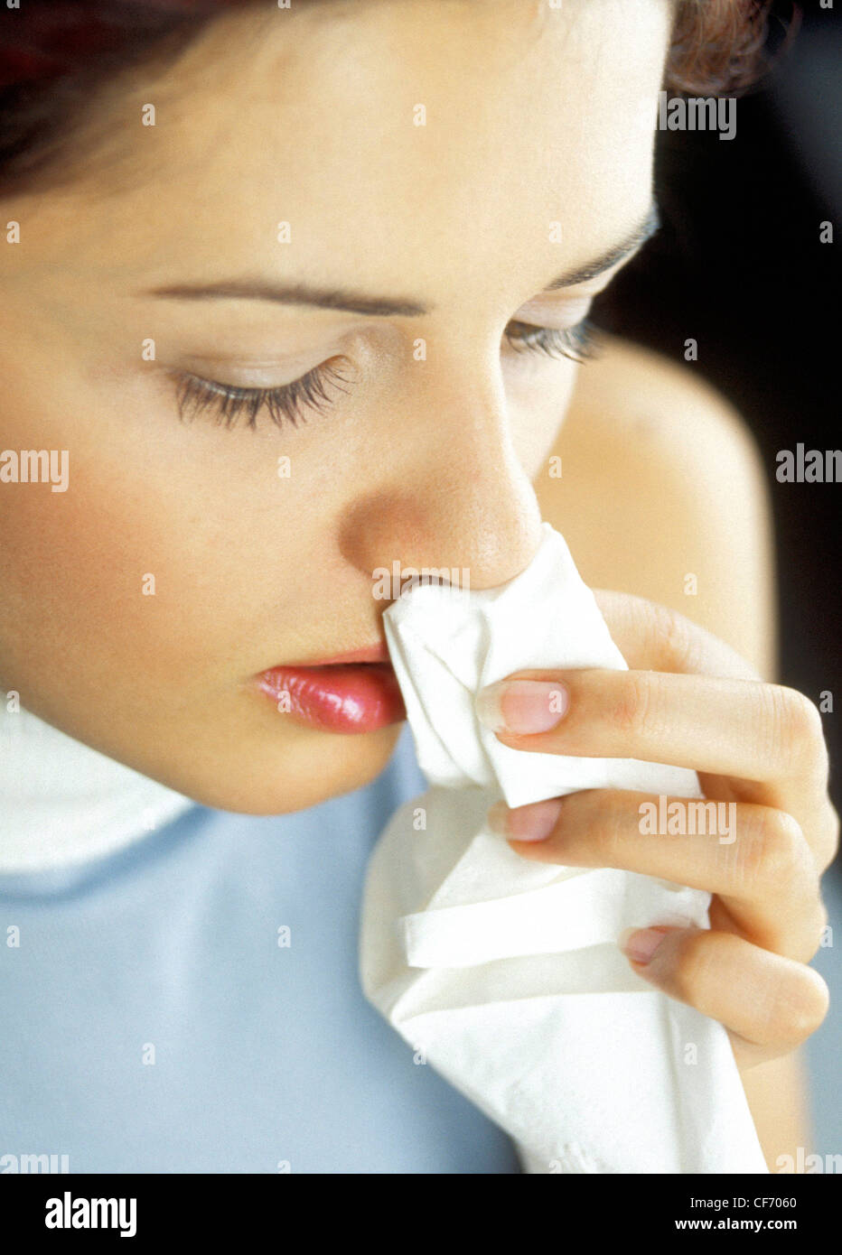 Cropped image of a brunette female wiping nose with a tissue, wearing ...