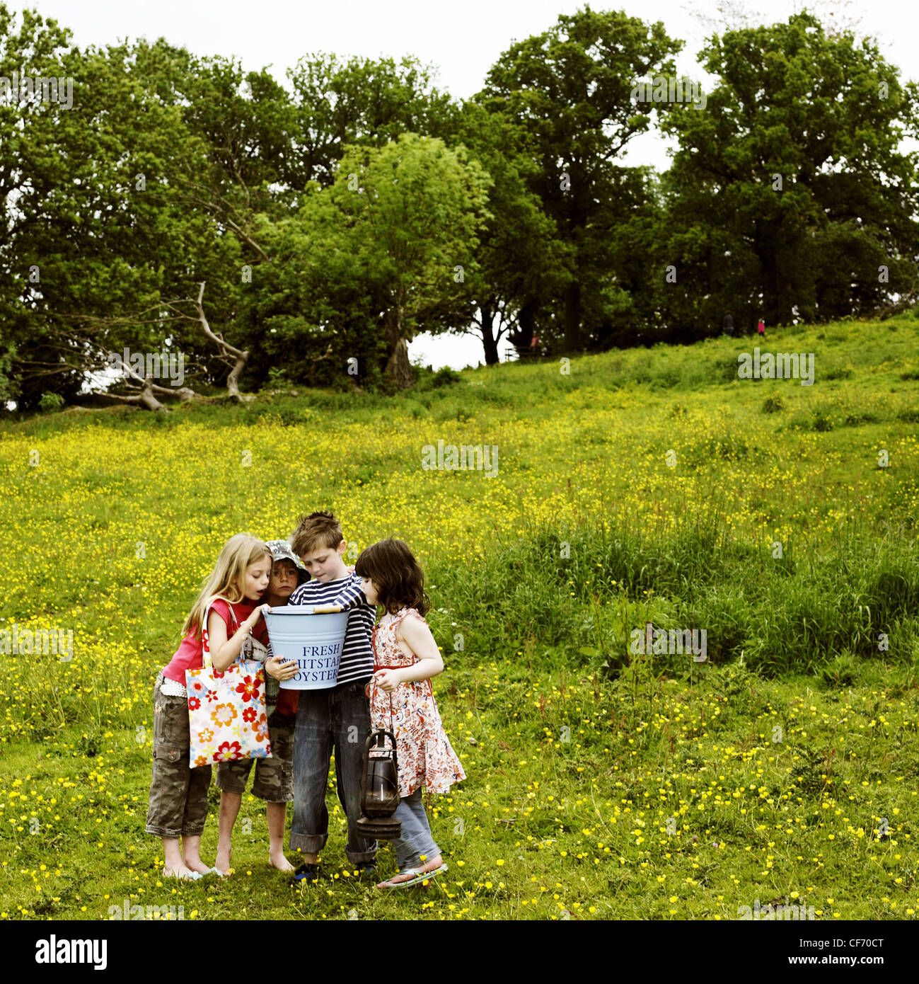 Four children in a field looking in a large blue bucket held by boy ...