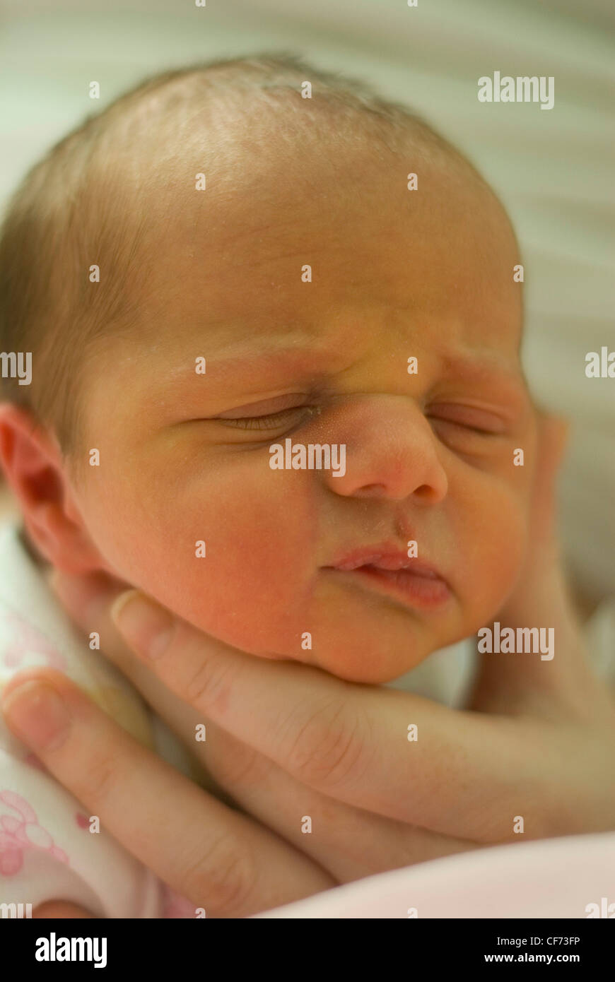 A newborn female baby dressed a white babygrow, with its head being ...