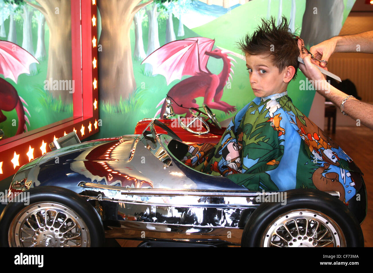 Eight year old male child sitting in a shiny toy car having his hair ...