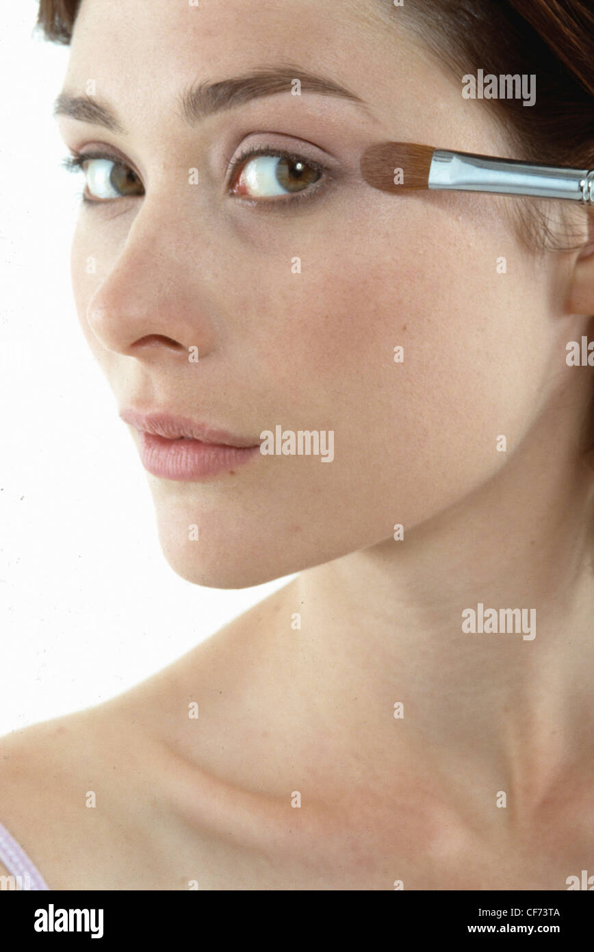 A close up image of female's face, applying shimmering eyeshadow with ...