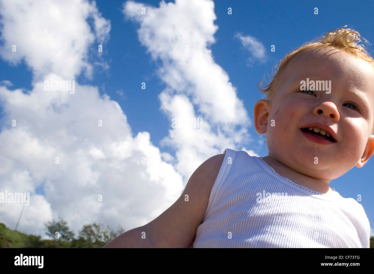 Male baby with blonde hair, wearing a white vest, standing on the beach ...