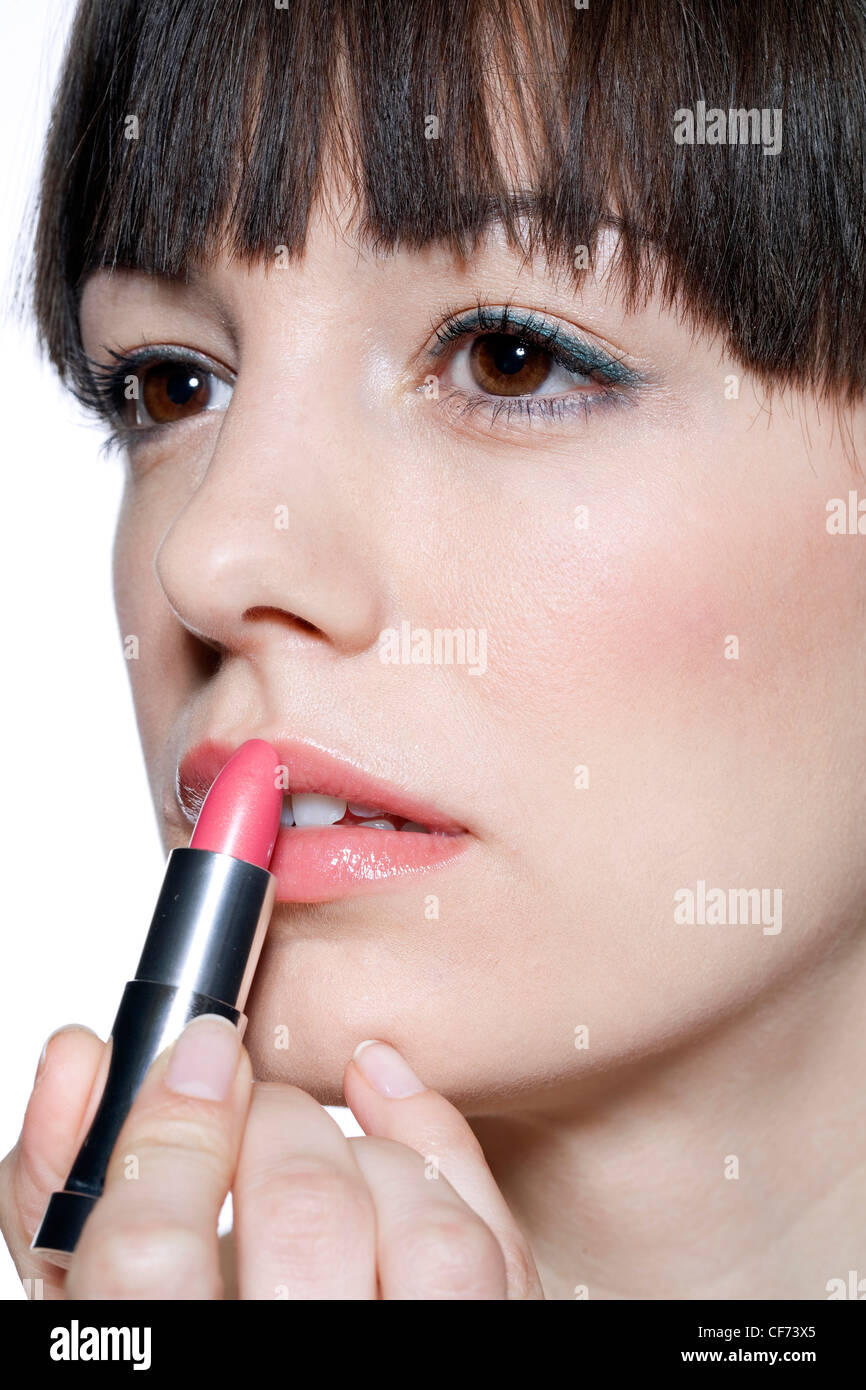 Female with fringed brunette hair, applying pink lipstick to her lips ...