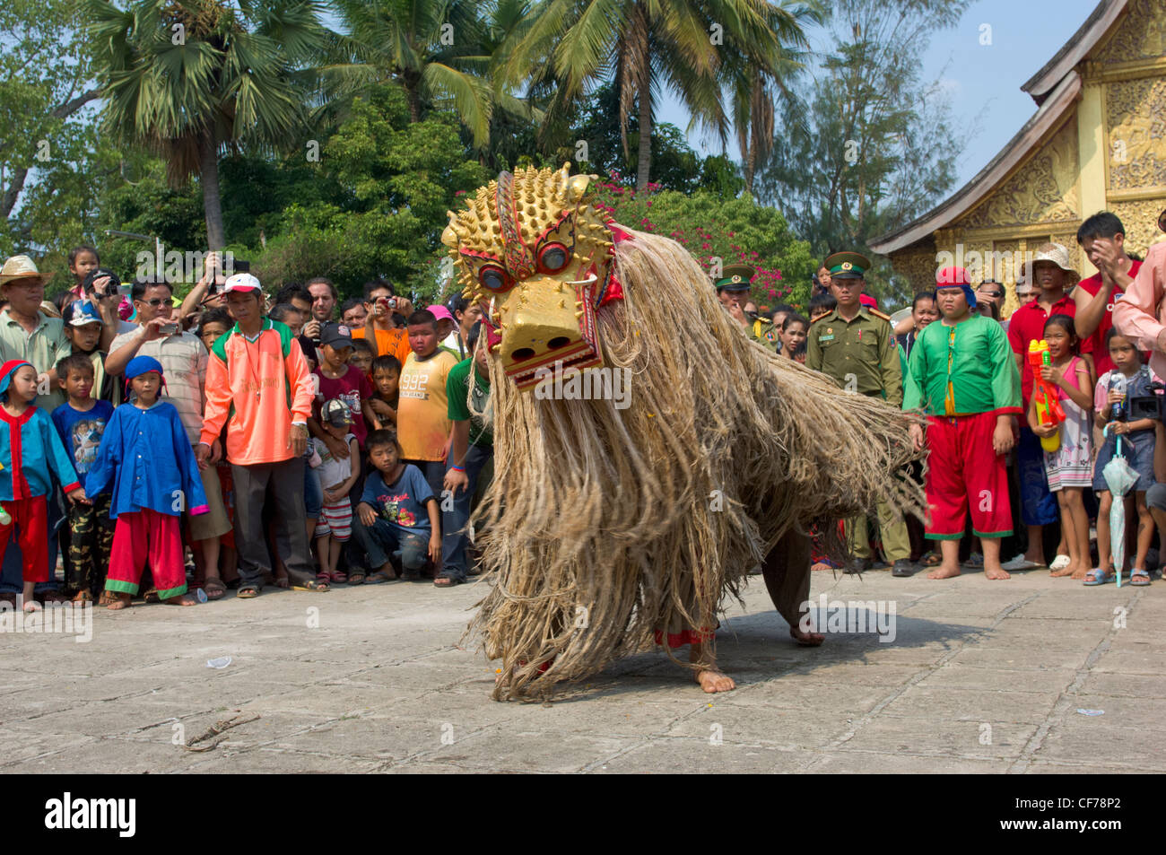 Mythical masked lion figure dancing in front of golden Sim, Wat Xieng ...