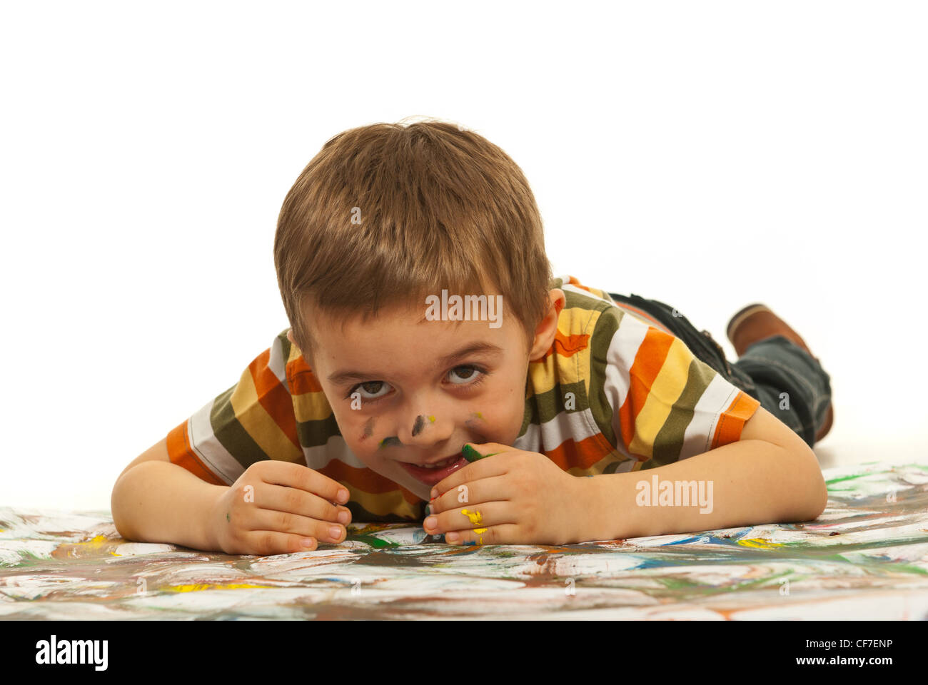 Messy happy boy trying to hide and laying down on painted background ...