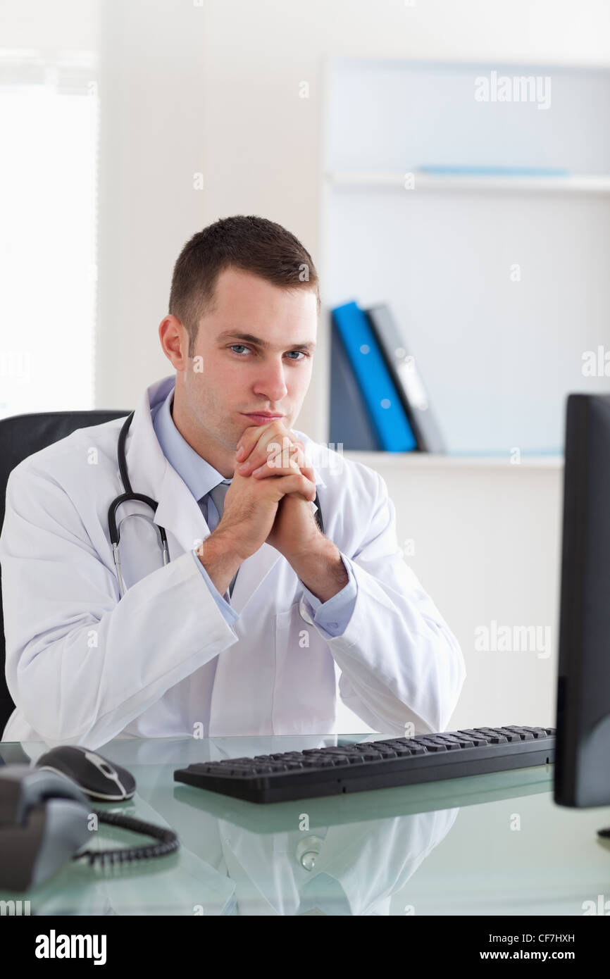 Thinking doctor sitting behind desk Stock Photo - Alamy