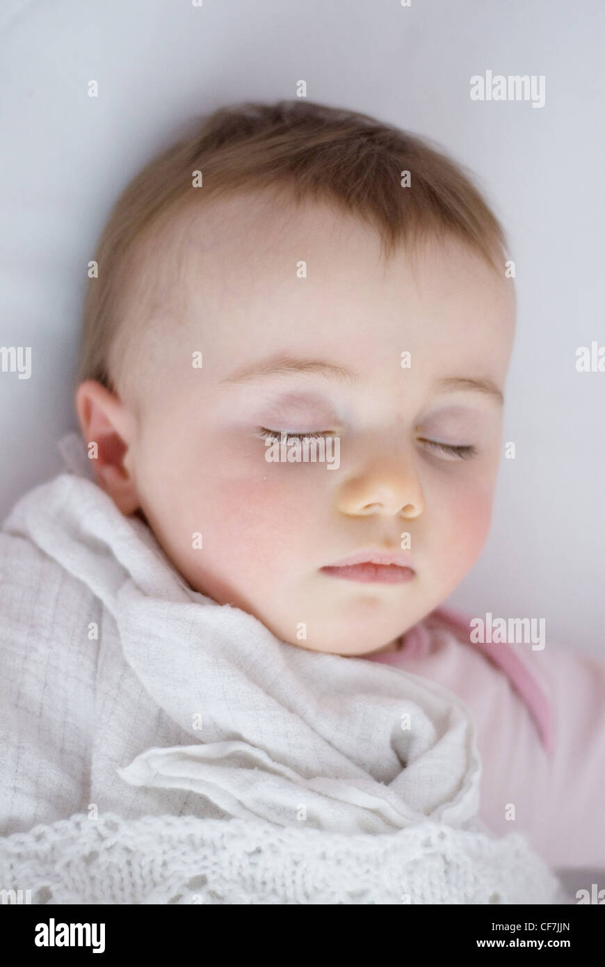 A female baby with fair hair, wearing a pink babygro, sleeping on her ...