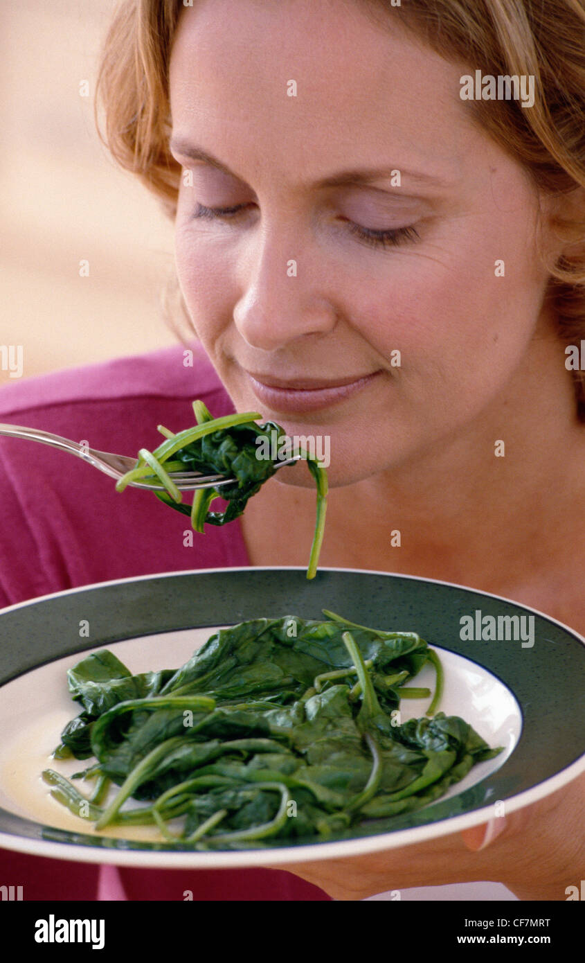 Female with short fair hair, wearing a pink cardigan, eating spinach ...