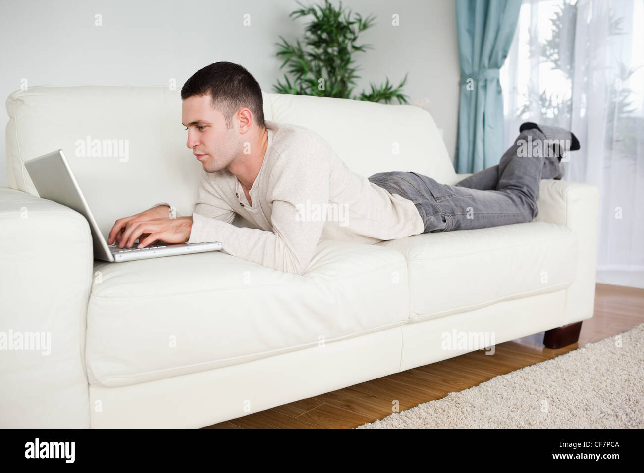 Handsome man lying on a couch using a laptop Stock Photo - Alamy