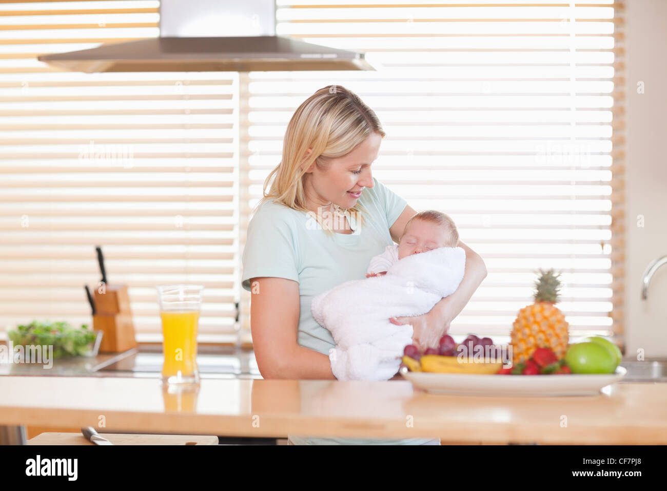 Woman holding her sleeping baby in the kitchen Stock Photo - Alamy