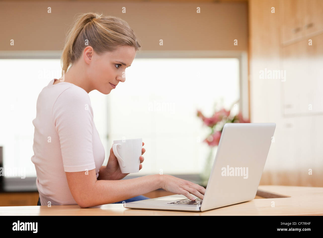 Woman using a laptop while drinking a cup of a tea Stock Photo - Alamy