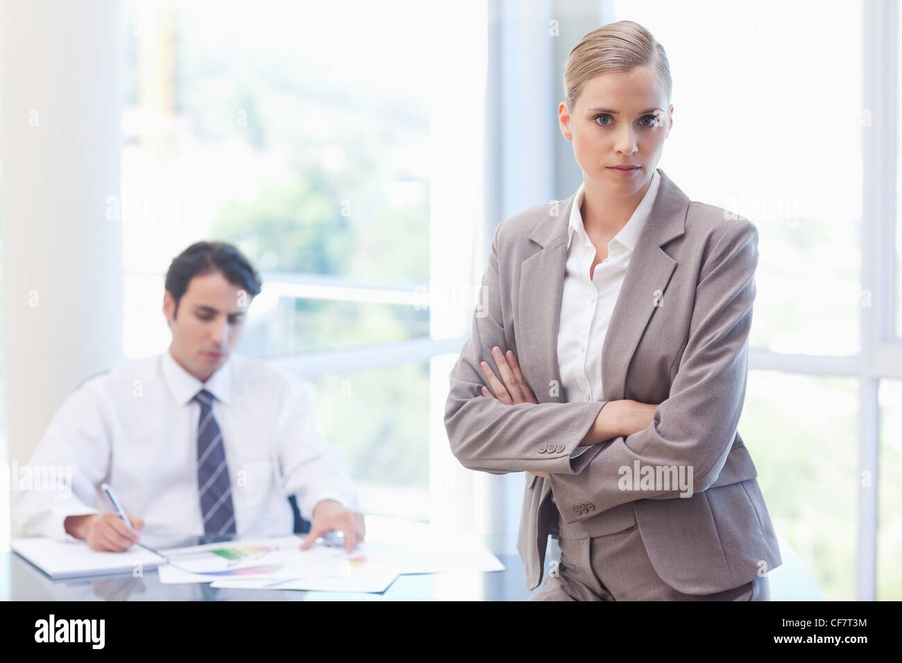 Serious businesswoman posing while her colleague is working Stock Photo ...