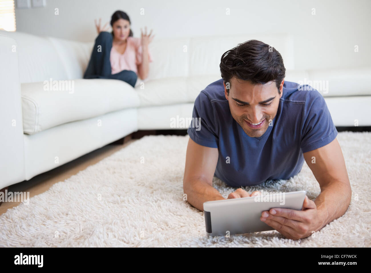 Man using a tablet computer while his girlfriend is getting mad at him ...