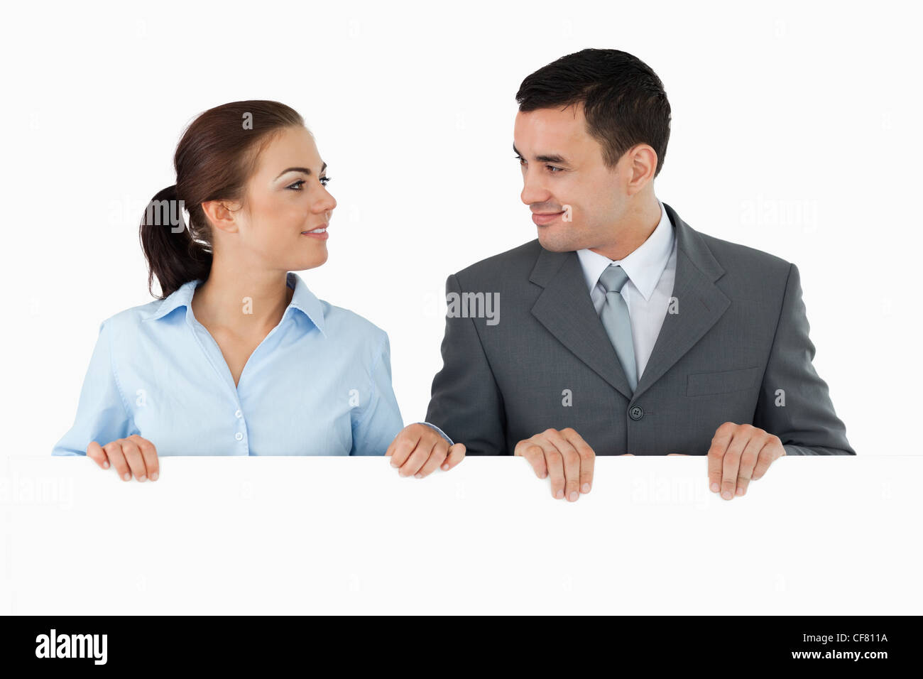 Business partners looking at each other while holding sign together ...