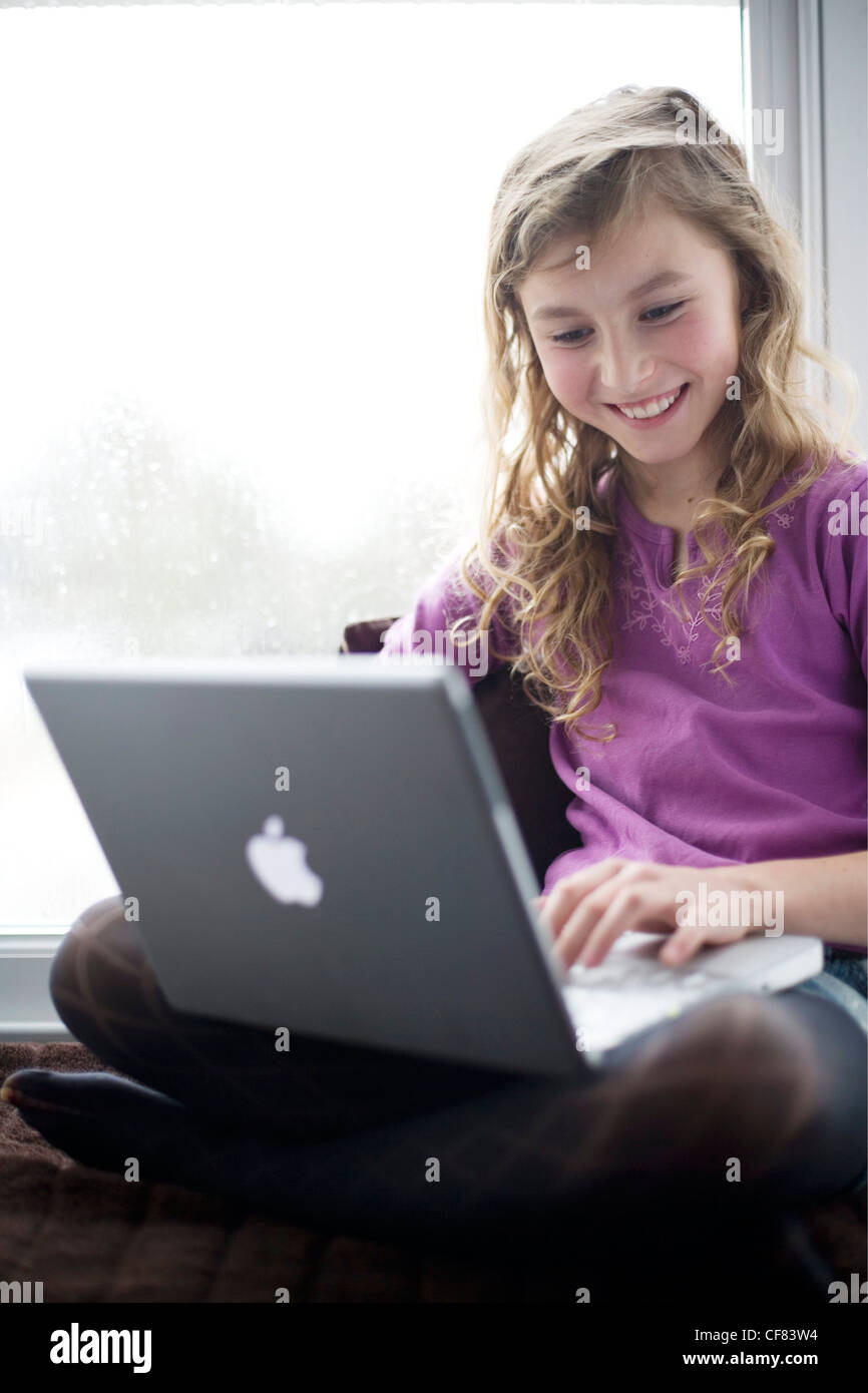 Blonde teenage female sitting cross legged with a laptop computer on ...