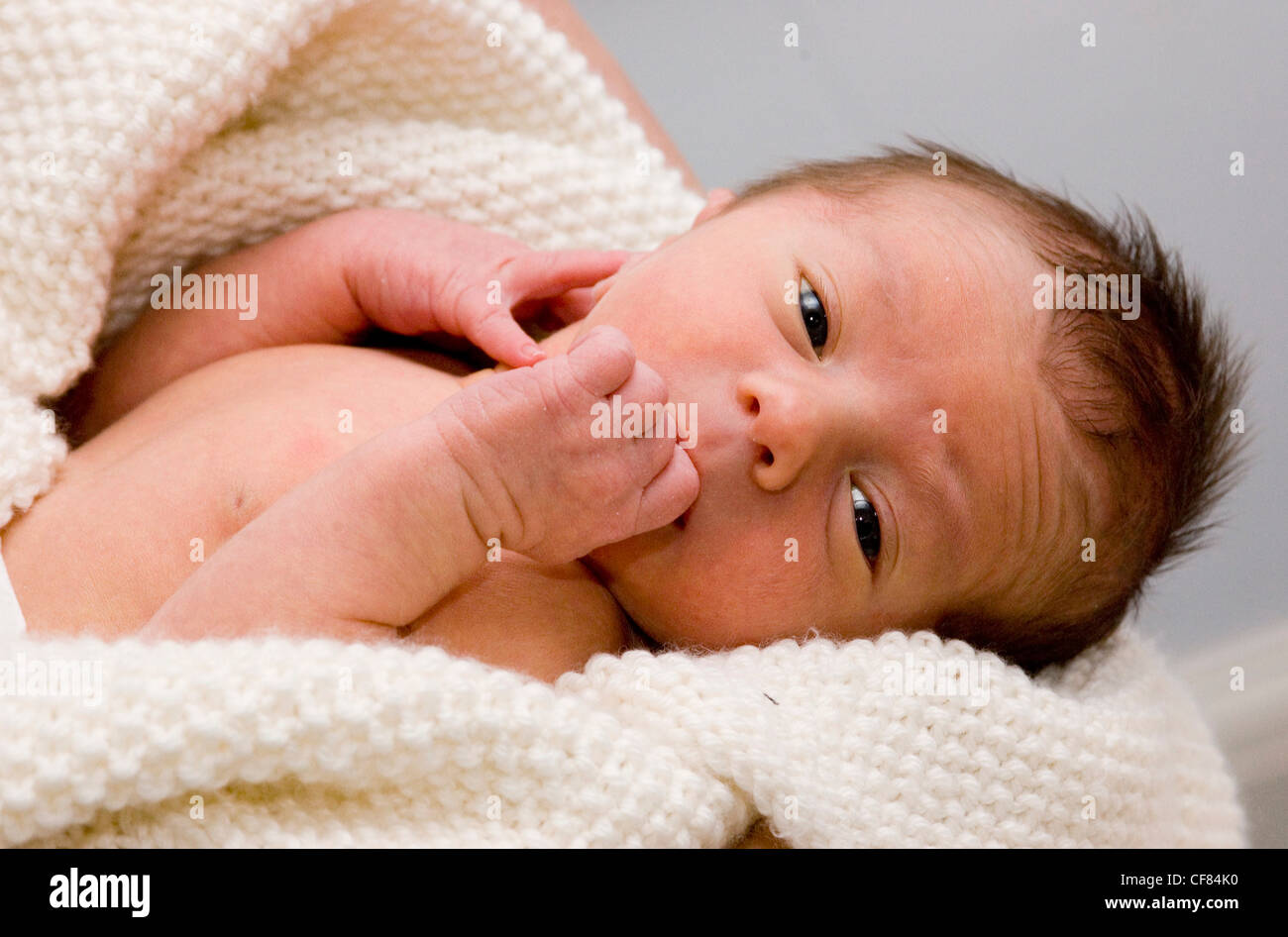 A newborn baby, lying on his back with head turned towards camera, with ...