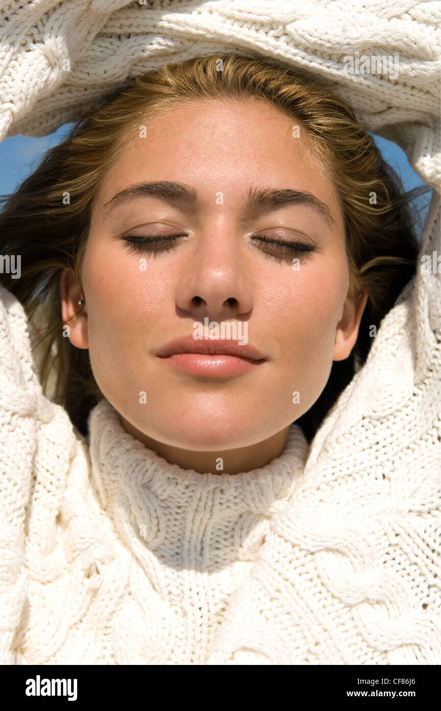 Female with blonde hair off face wearing cream knitted jumper arms up ...